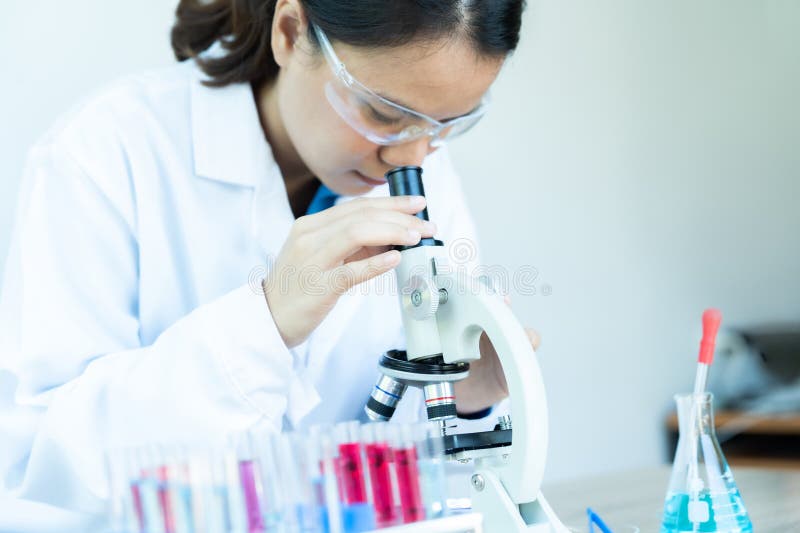 A Woman in a Lab Coat is Looking through a Microscope. Concept of ...