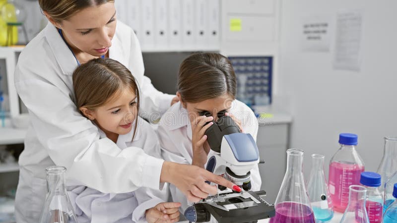 A Woman in a Lab Coat Supervises Two Young Girls Using a Microscope in ...