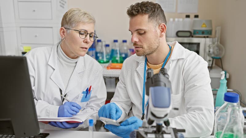 A Woman and a Man in Lab Coats Work Collaboratively in a Scientific ...