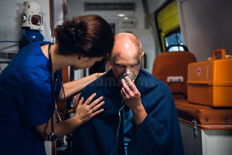 Woman In Medical Uniform Stands With Man Who Sits In Oxygen Mask In
