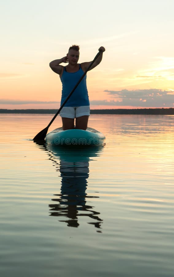 A Woman With A Mohawk In Shorts On Her Knees On A Sapboard With An Oar