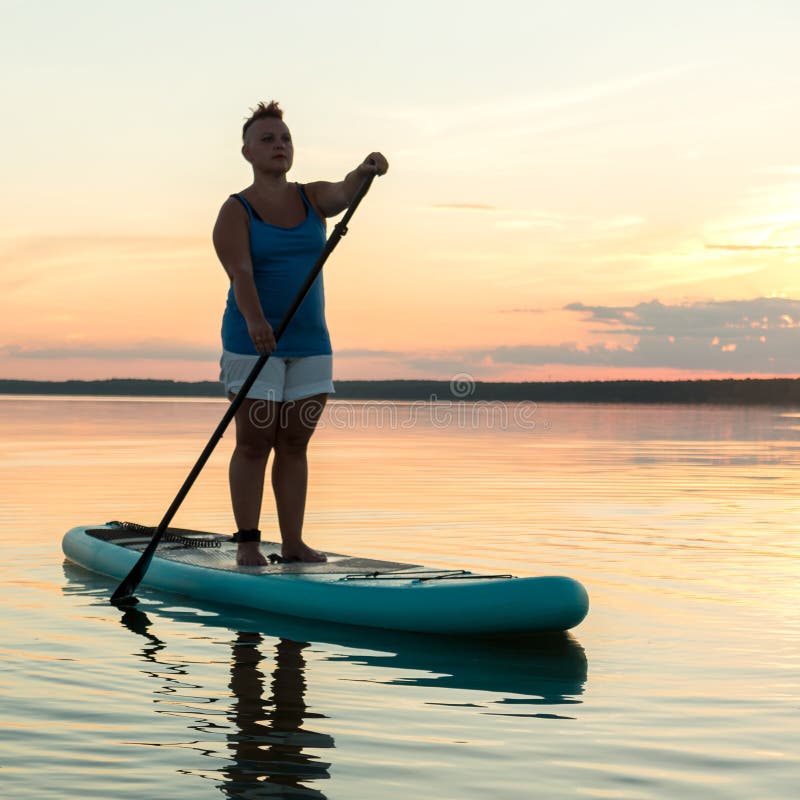 A Woman With A Mohawk In Shorts On A Sapboard With An Oar Against The