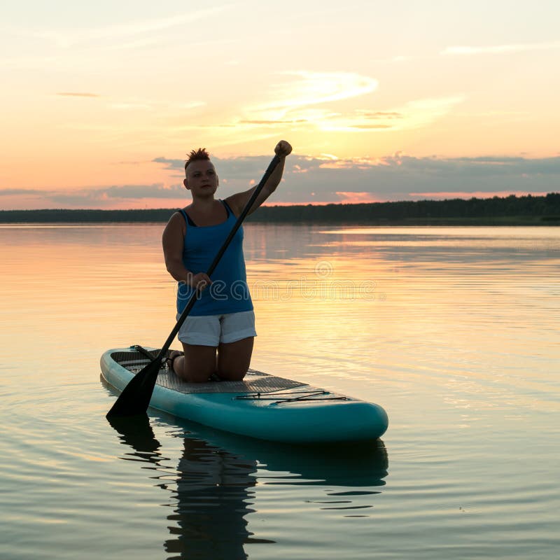 A Woman With A Mohawk In Shorts On A Sapboard With An Oar Against The