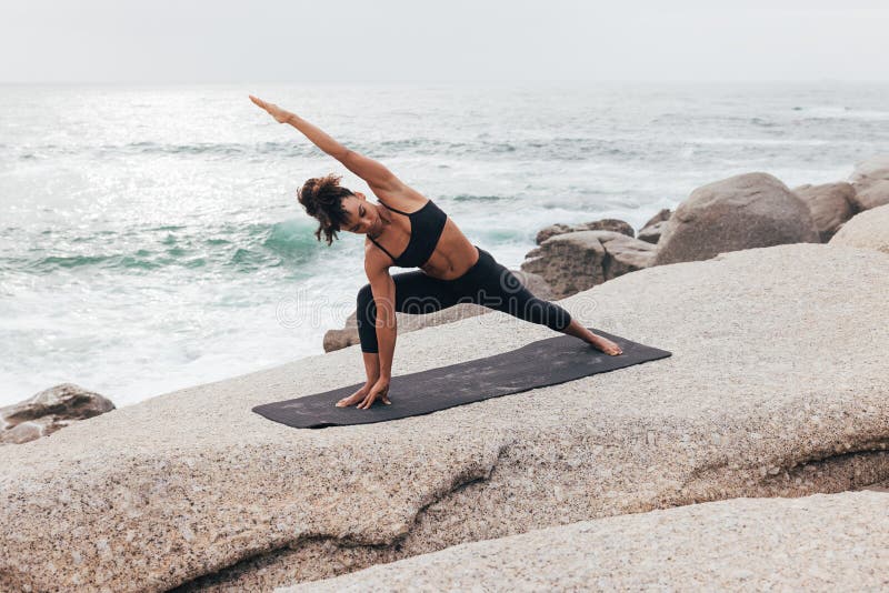 Woman Practicing Extended Side Angle Pose by Ocean at Sunset Stock ...