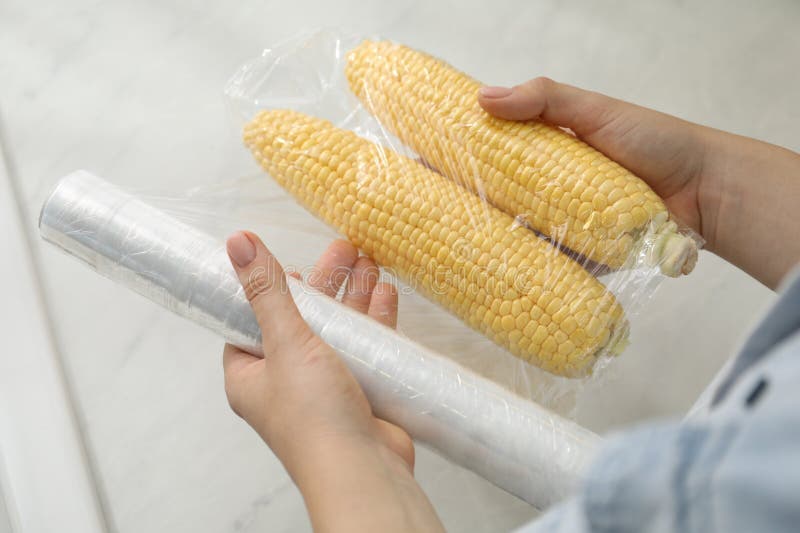 Woman Putting Plastic Food Wrap Over Corncobs in Kitchen, Closeup Stock ...