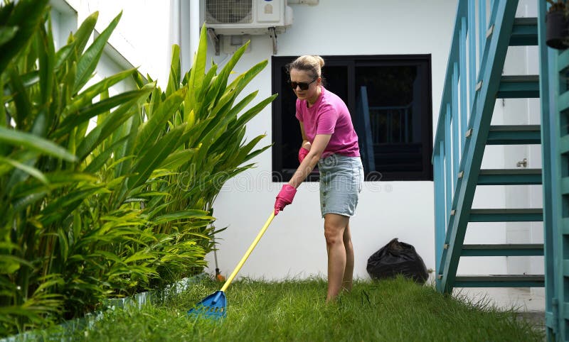 A Woman Raking the Lawn at the Backyard of Her House Stock Image ...
