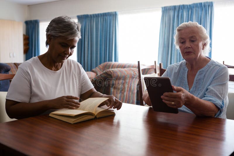 Woman Reading Book while Friend Using Tablet at Table Stock Image ...