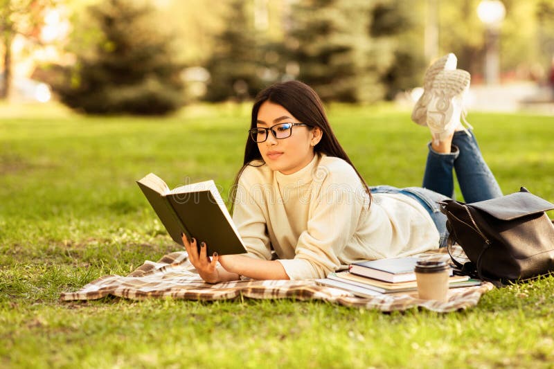 Woman Reading Book While Laying On Grass Enjoying Sunny Day Stock