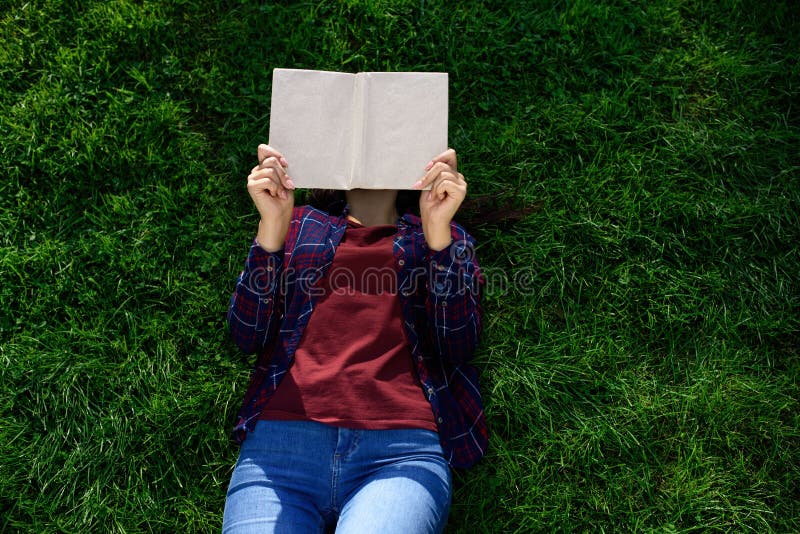 Woman Reading Book while Lying on Green Grass Outdoors, Top View Stock ...