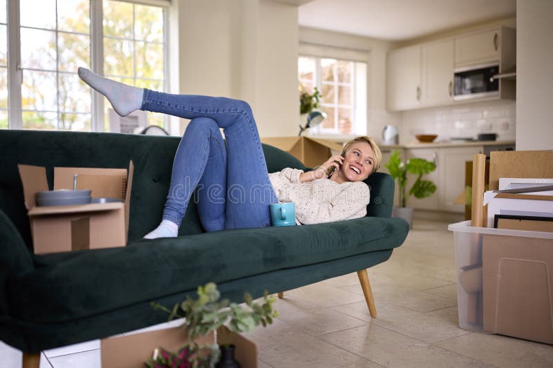 Woman Relaxing on Sofa Using Mobile Phone Surrounded by Unpacking Boxes ...