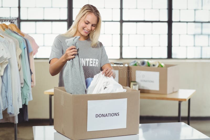 Woman Volunteer Sorting Garments from Donation Box on Table at Donation ...