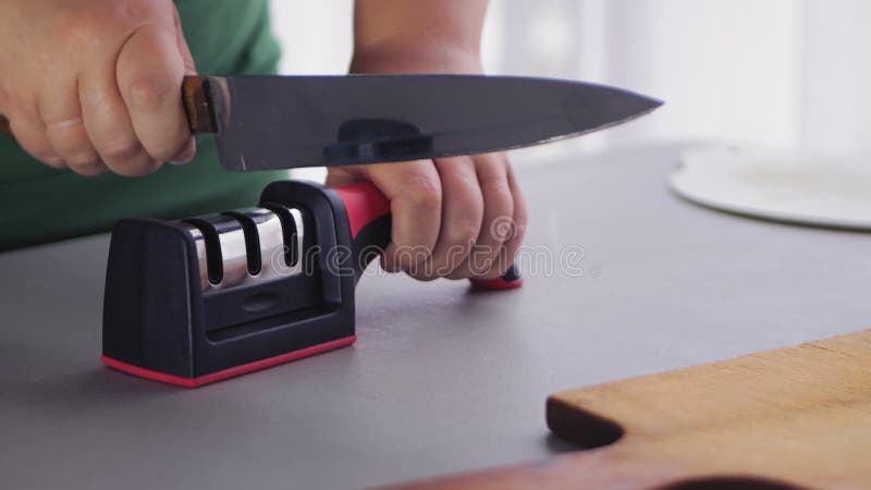 A Woman Sharpens a Kitchen Knife in a Knife Sharpener on the Table ...