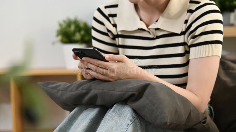 A Woman is Sitting on a Couch and Using Her Cell Phone Stock Photo ...