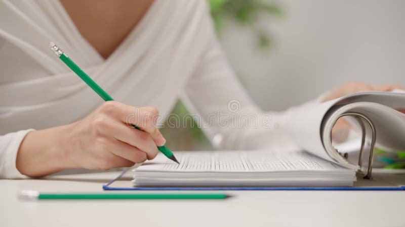 Woman Sitting at Office Desk Sorting and Signing Stack of Paper Document Sheets with Pencil in ...