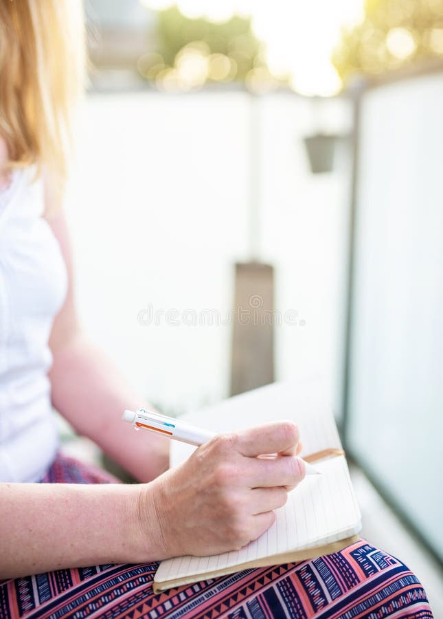 Woman Sitting on Patio Taking Notes in Notebook Stock Photo - Image of ...
