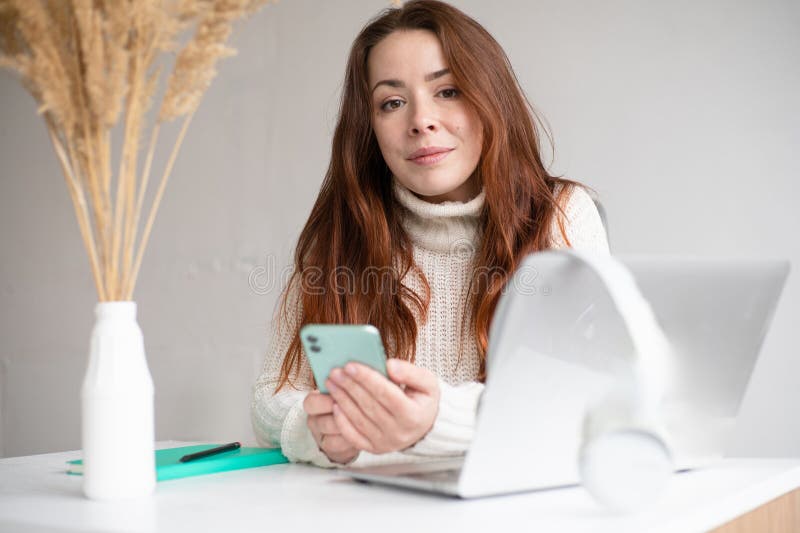 Woman Sitting at Table Holding Smartphone, Looking at Camera while ...