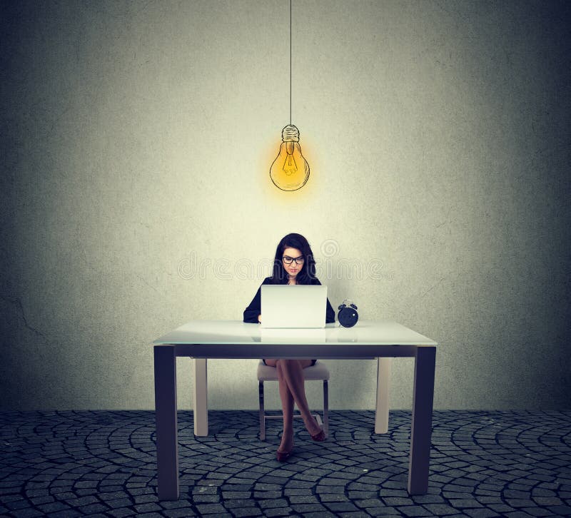 Woman Sitting at Table Working on Laptop with Bright Light Bulb Above ...