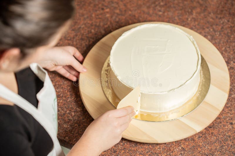 Woman Smoothing Edges of a Chocolate Cake Covered with Whipped Cream, Using a Cake Smoother Tool ...