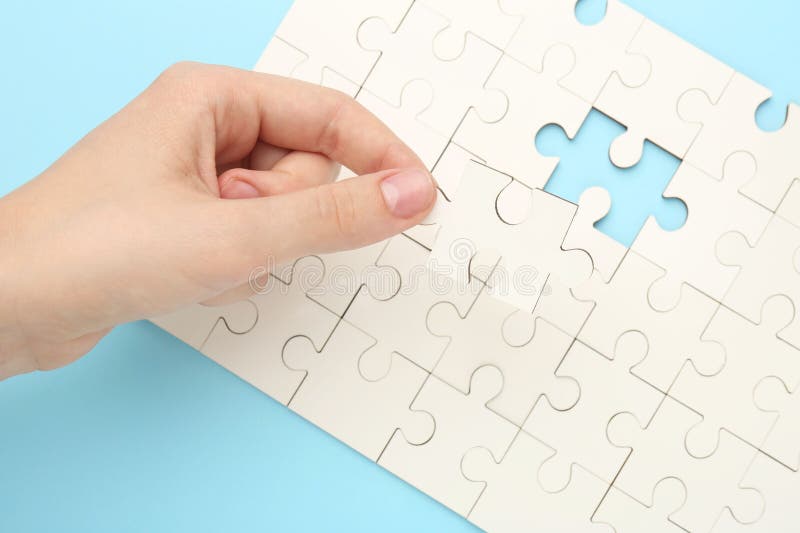 Woman Solving White Puzzle on Light Blue Background, Closeup Stock ...
