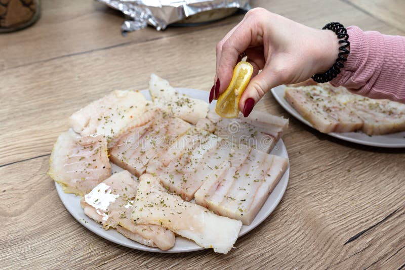 A Woman Squeezes Lemon on a Fresh Cod Fillet Cut into Squares ...