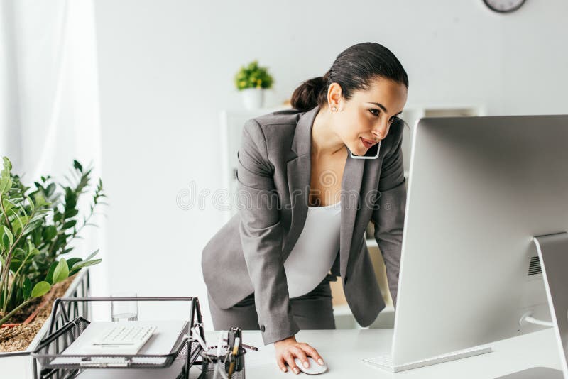 Woman Standing Near Table, Working on Computer and Talking on ...