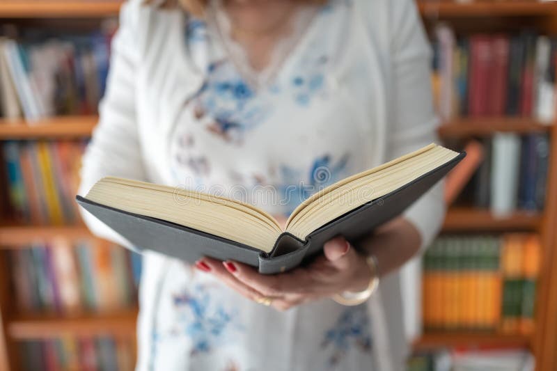 Woman Standing with an Open Book while Reading with a Large Bookcase ...