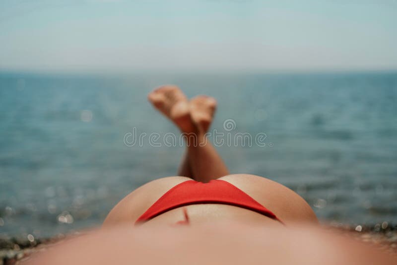 A Woman Sunbathes On The Beach Lying On Her Stomach In A Red Swimsuit