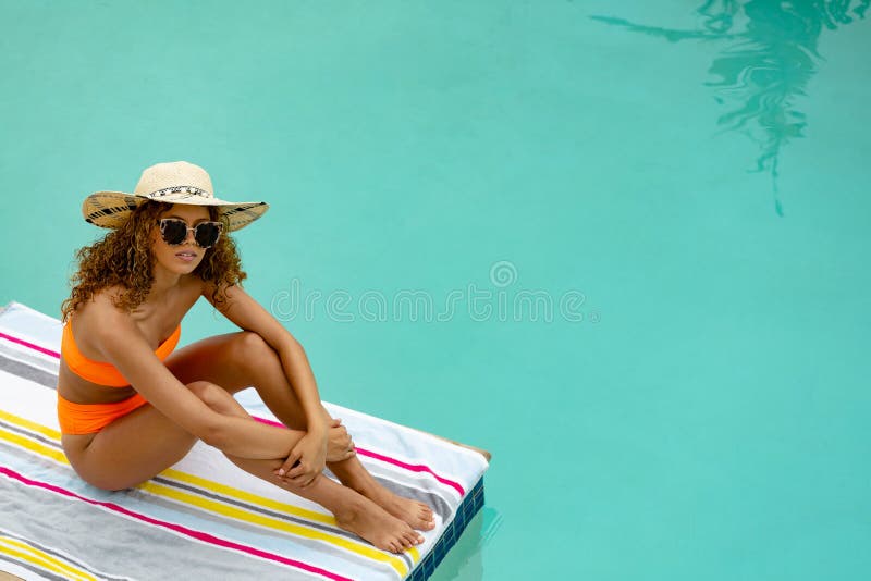 Woman In Sunglasses And Hat Sitting At The Edge Of Swimming Pool Stock