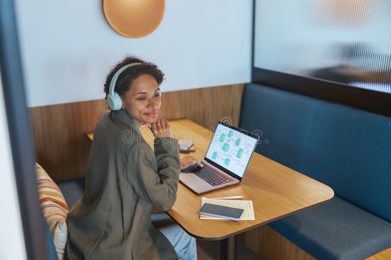 A Woman at a Table with a Laptop, Headphones on, Using a Personal ...