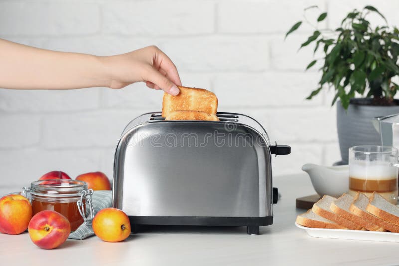 Woman Taking Roasted Bread Out of Toaster at White Table, Closeup Stock ...
