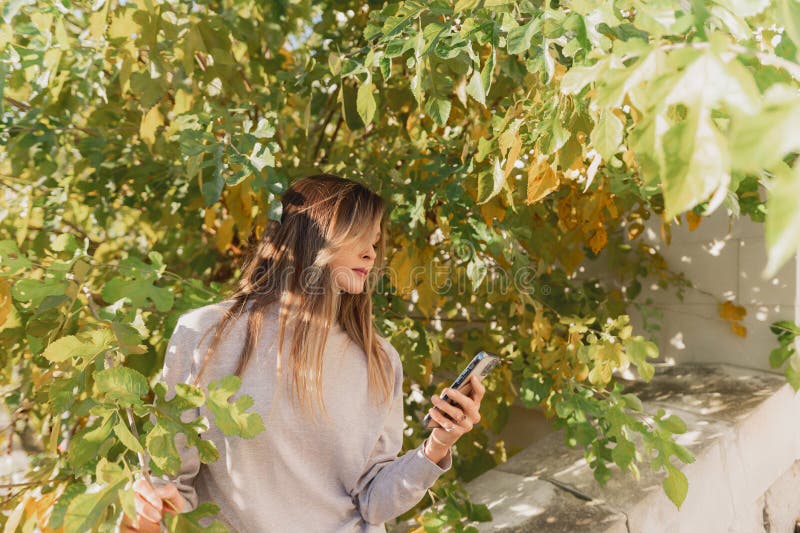 A Woman is Talking on Her Cell Phone while Sitting Under a Tree. she is ...