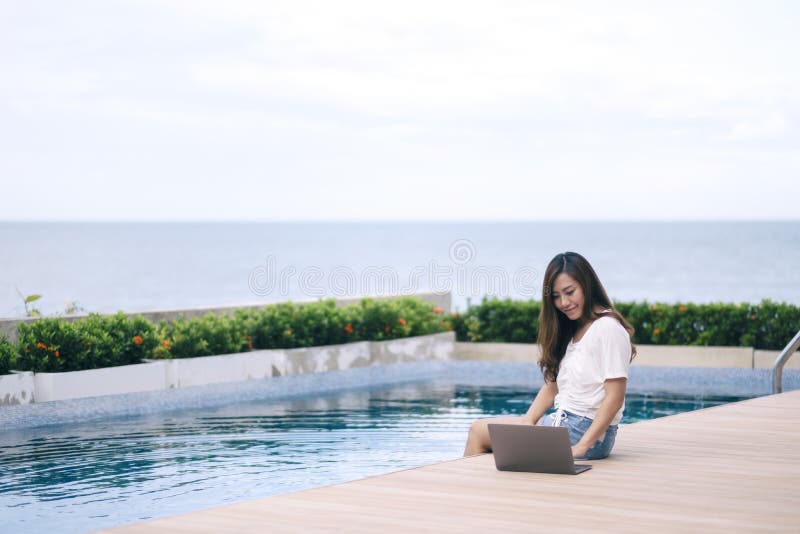 Woman Using and Typing on Laptop Computer while Sitting by Swimming ...