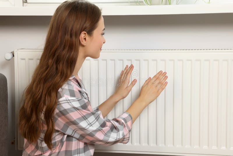 Woman Warming Hands on Heating Radiator Near White Wall Stock Image ...