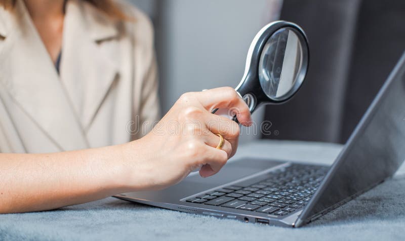 Woman Working on a Laptop and Using a Magnifying Glass To Look at Data ...
