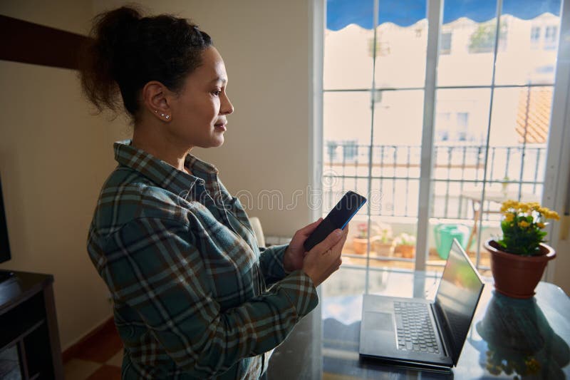 Woman Working Remotely Using a Phone and Laptop in Bright Home Office ...