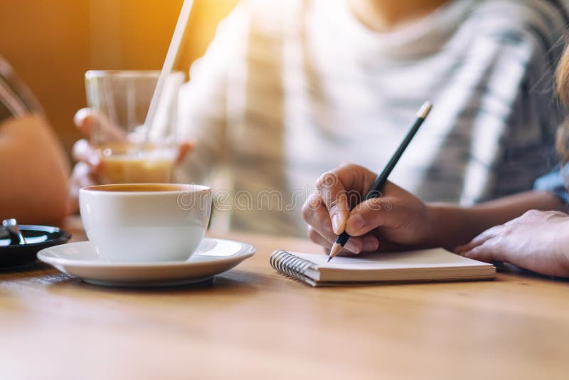 A Woman Writing on a Notebook while Drinking Coffee with Friends Stock ...
