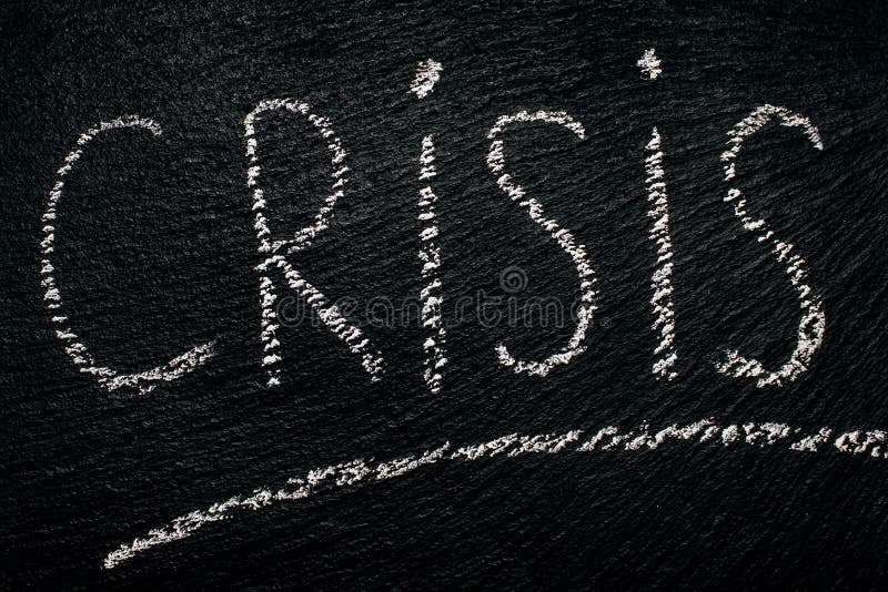 The Word Crisis is Written in White Chalk on a Black Rough Surface and ...