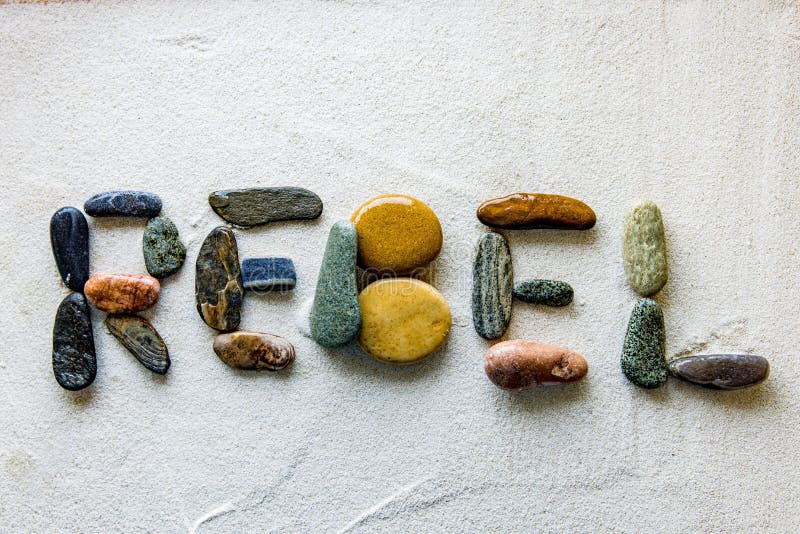 Word REBEL is Written Using Colored Stones on a White Sand Surface ...