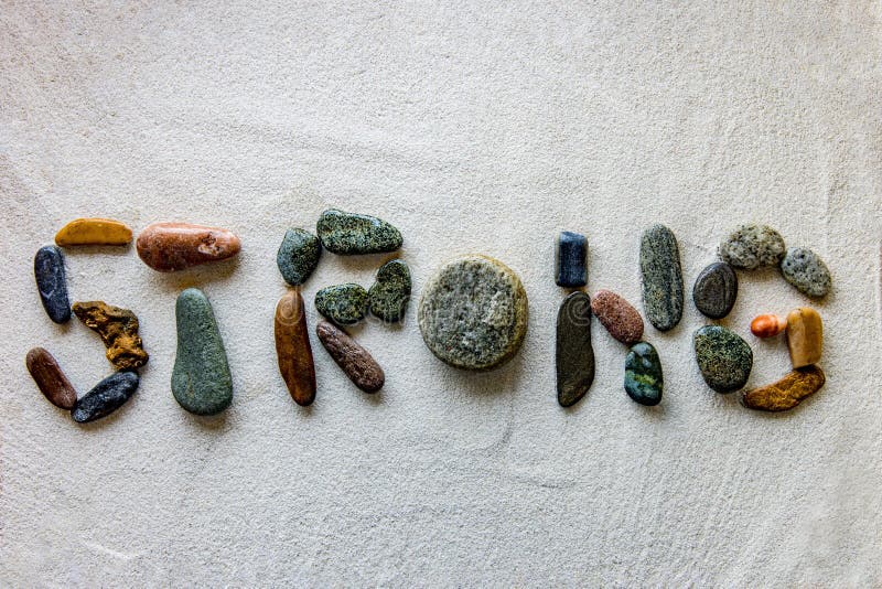 Word STRONG is Written Using Colored Stones on a White Sand Surface ...