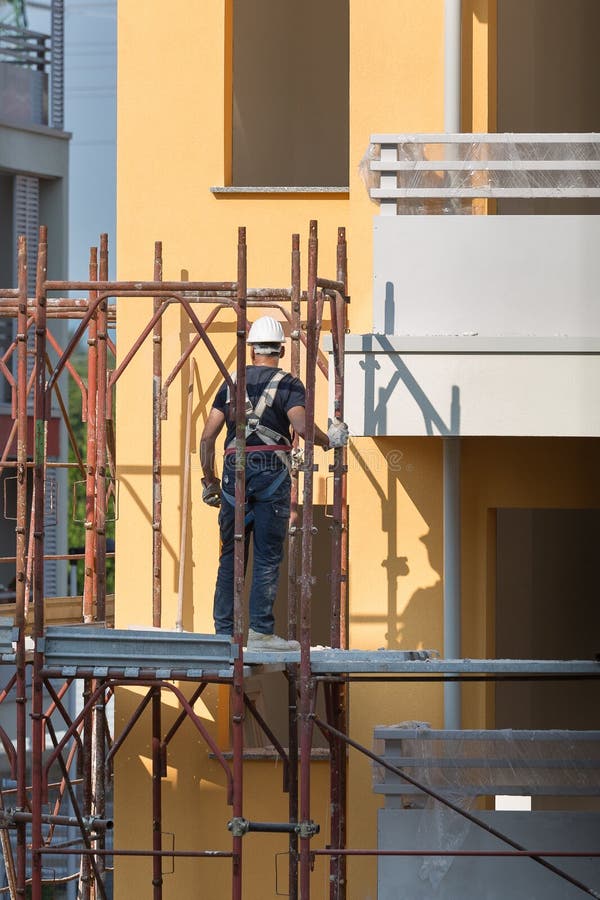 Worker with Blue Hardhat at Work on a Scaffold in a Building Site for ...