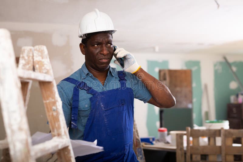 Worker in Blue Overalls Communicates on a Mobile Phone in Renovated ...