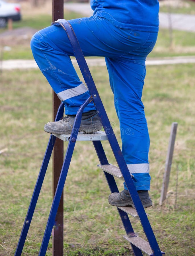 Worker in Blue Overalls Stands on a Metal Ladder in the Yard Stock ...