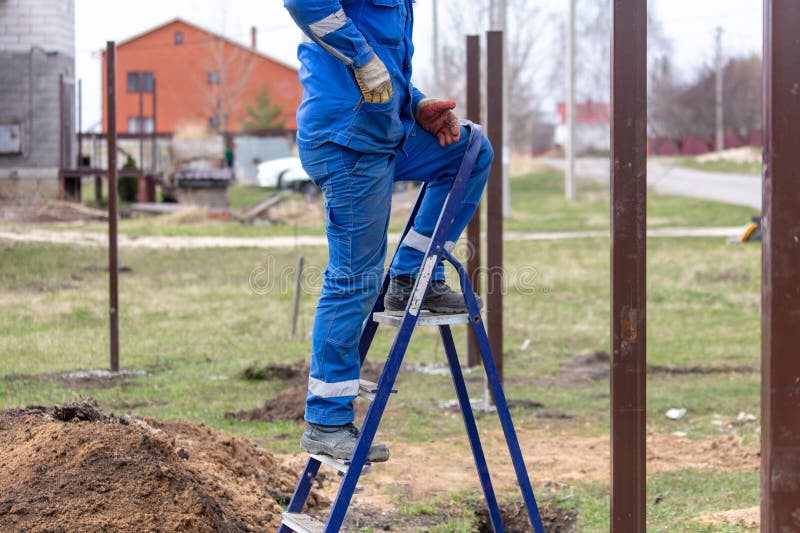 Worker in Blue Overalls Stands on a Metal Ladder in the Yard Stock ...
