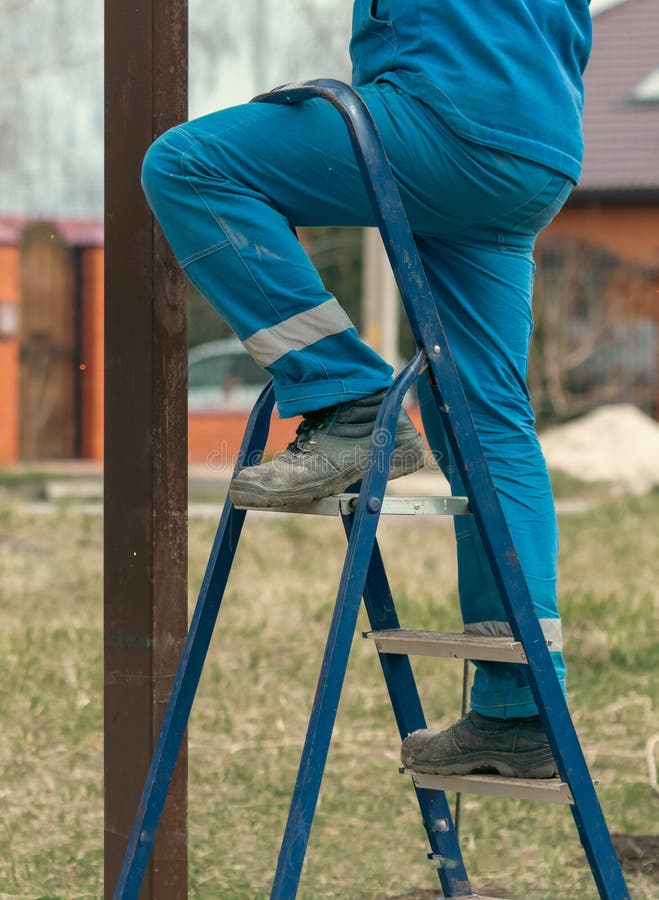 Worker in Blue Overalls Stands on a Metal Ladder in the Yard Stock ...