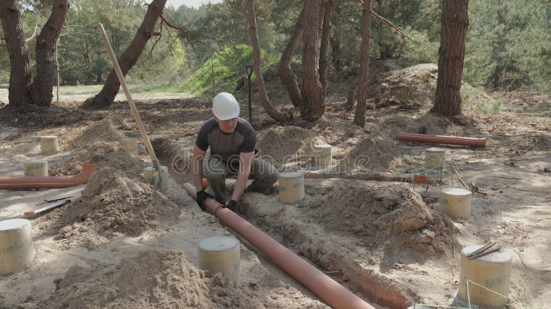 Construction Worker Laying Underground Pipes in a Forested Area during ...