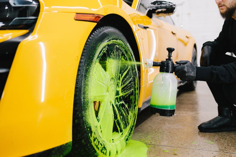 Worker Cleans the Tire of a Yellow Car Using a Spray with Soap Solution ...