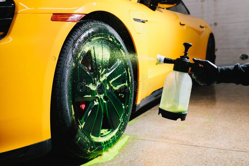 Worker Cleans the Tire of a Yellow Car Using a Spray with Soap Solution ...