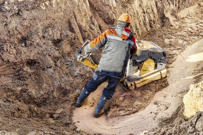 A Worker Compacts Soil or Sand with a Vibrating Plate in a Trench at a ...