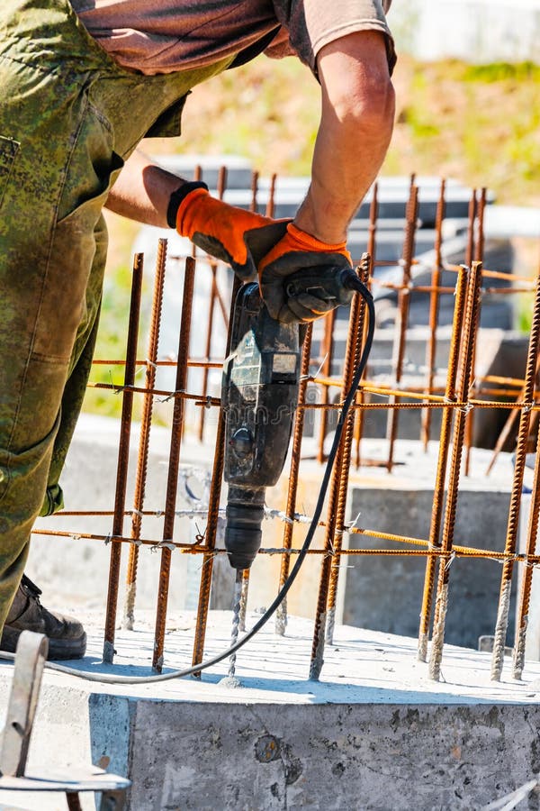 A Worker at a Construction Site Drills a Reinforced Concrete Foundation ...
