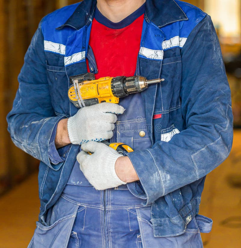 Worker in Dirty Uniform and Protective Gloves with Drill in His Hand in ...